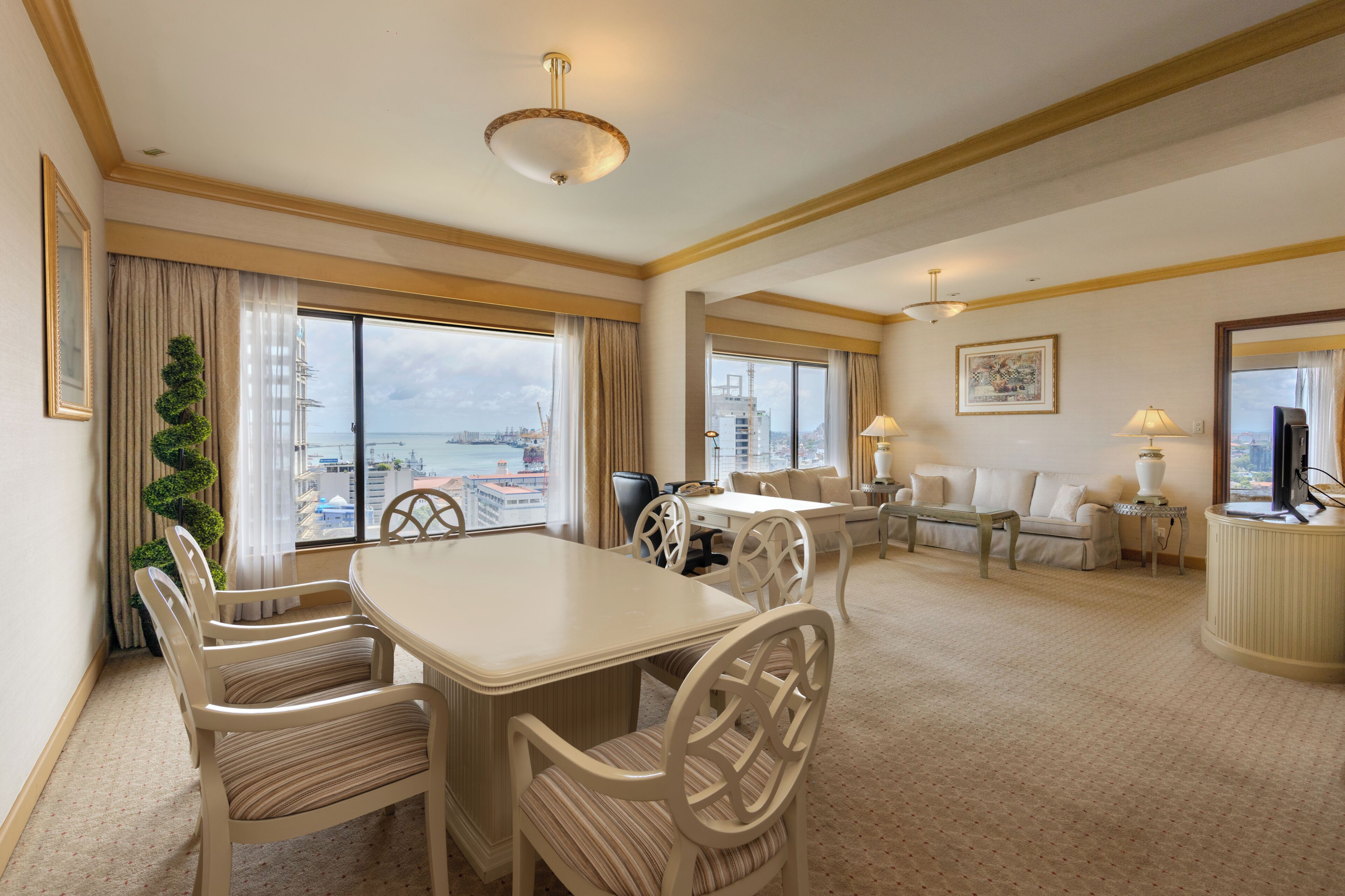 Quarto de hotel com área de jantar, sofás, televisão e vista para o mar.
