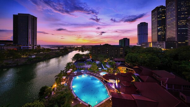 Um resort com uma piscina grande, um rio e edifícios altos ao fundo.