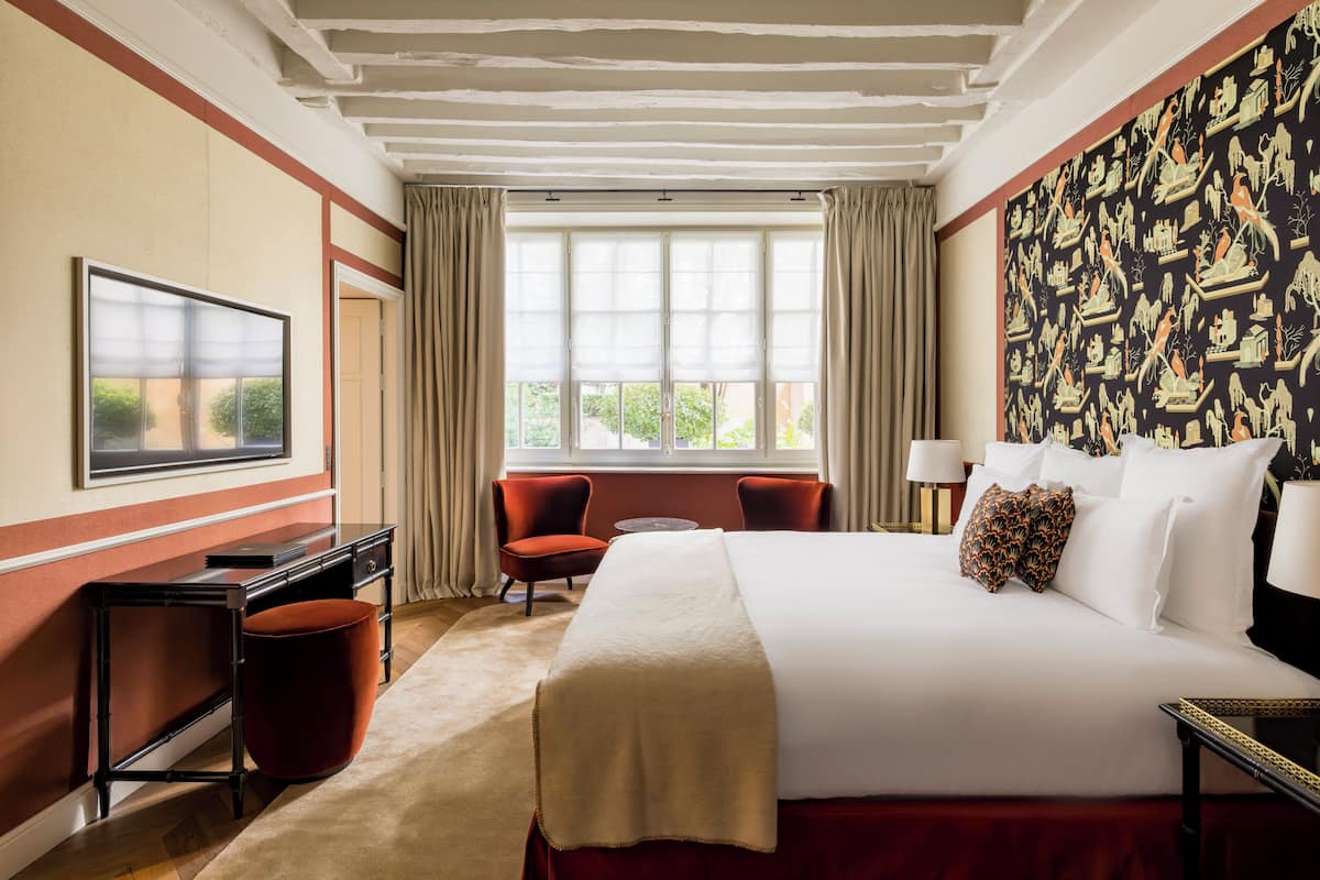 Quarto de hotel com uma cama grande, uma escrivaninha, uma cadeira e uma janela com cortinas.