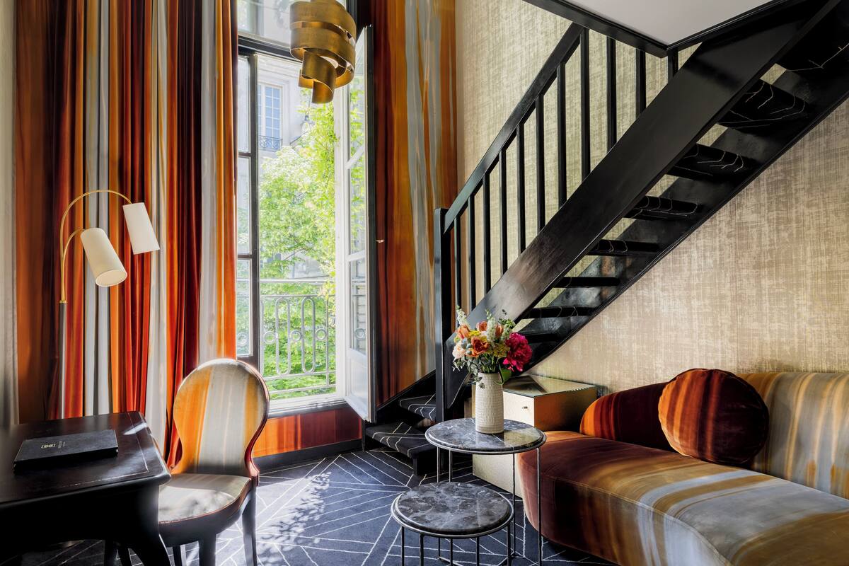 Quarto de hotel moderno com escada, sofá, mesa de jantar e uma cadeira.