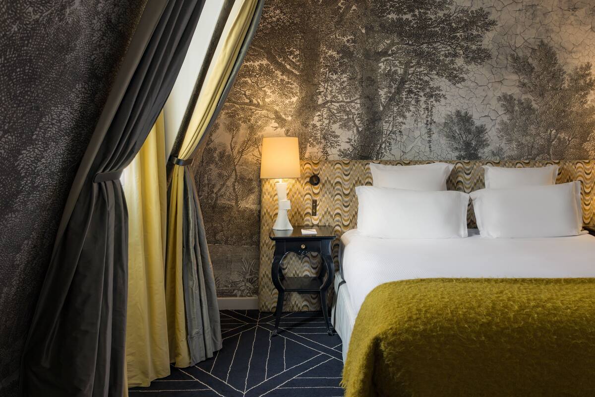 Quarto de hotel com uma cama, uma mesa de cabeceira com abajur e parede estampada.