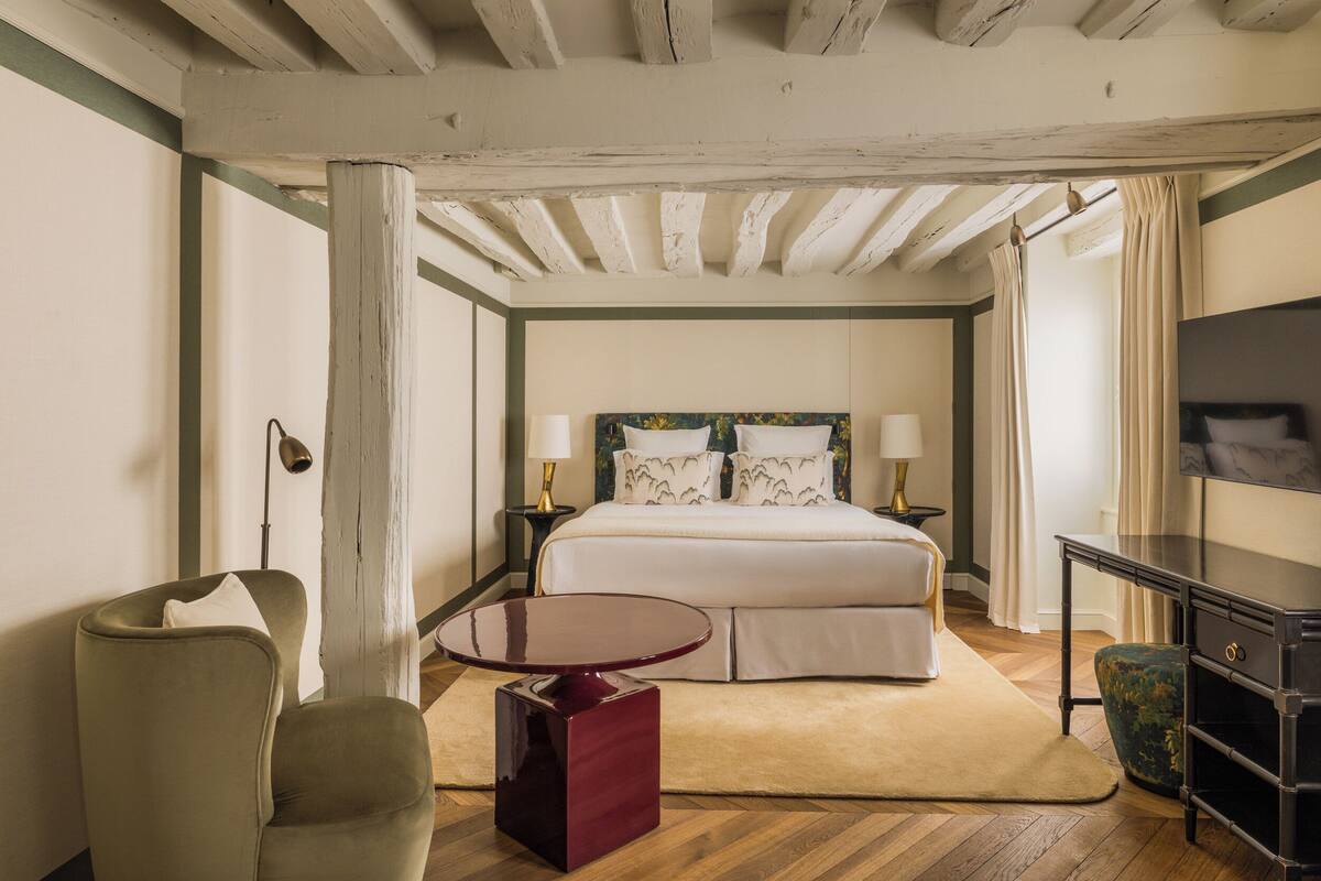 Um quarto com uma cama, mesas de cabeceira, uma cadeira, uma mesinha e uma televisão.