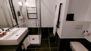 Uma casa de banho moderna com cabine de duche em vidro, uma sanita e uma pia branca.