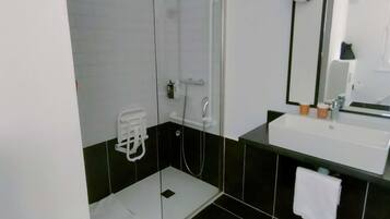 Casa de banho com chuveiro, pia, espelho e um porta-toalhas.