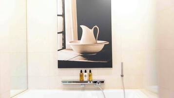 Casa de banho com banheira, chuveiro e prateleira na parede com artigos de higiene pessoal.