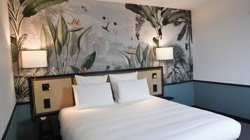 Quarto de hotel com uma cama grande, duas luminárias de cabeceira e um mural na parede com plantas e pássaros tropicais.