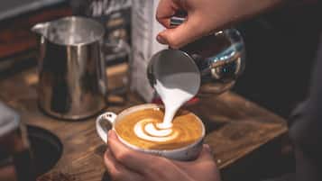 Alguém a verter leite numa chávena de café, criando um desenho artístico no latte.