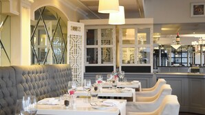 Um restaurante com assento acolchoado cinzento, mesas brancas com copos e design de interiores moderno.