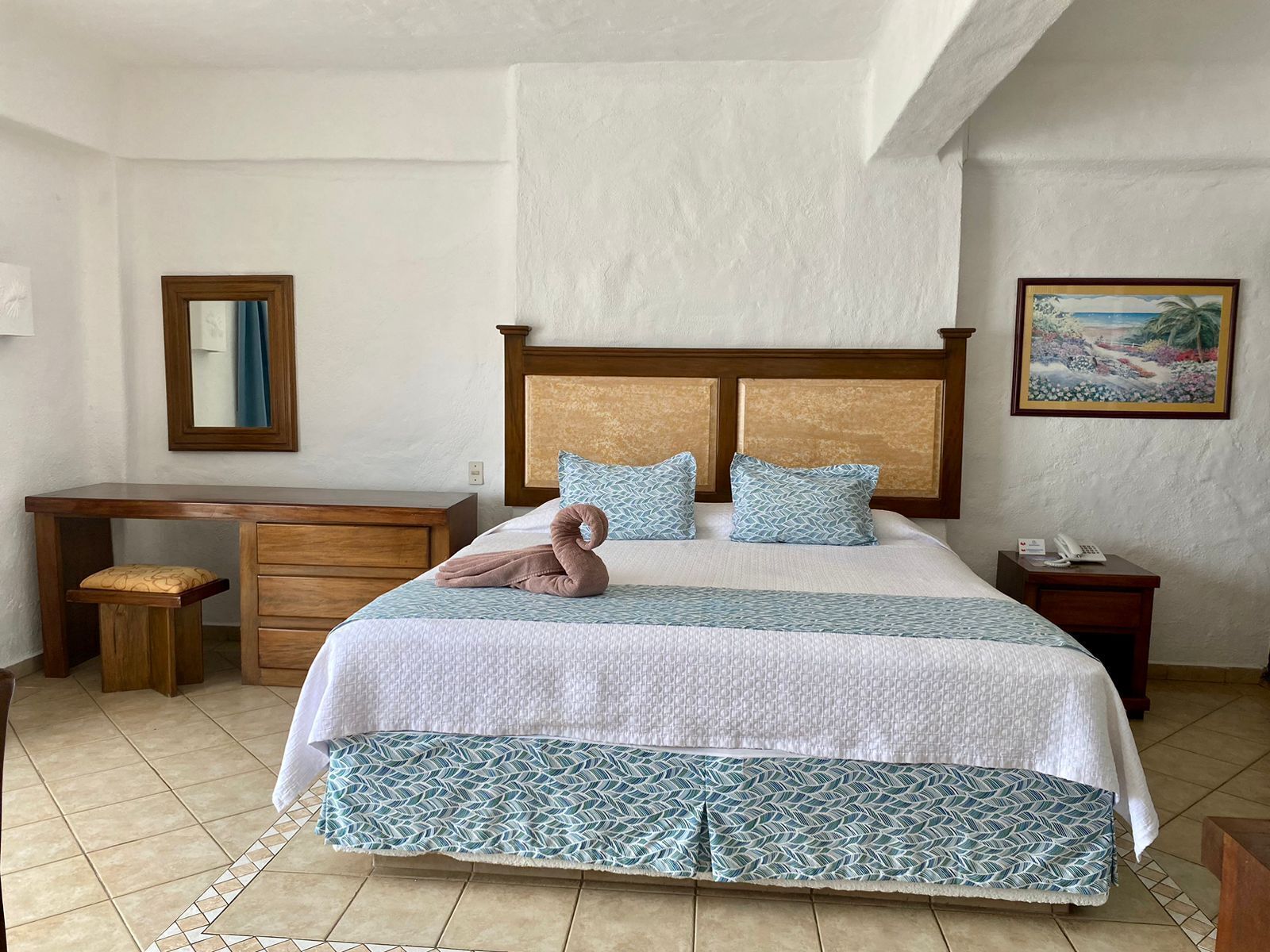 Quarto bem arrumado com cama, escrivaninha de madeira, cadeira e mesa de cabeceira.