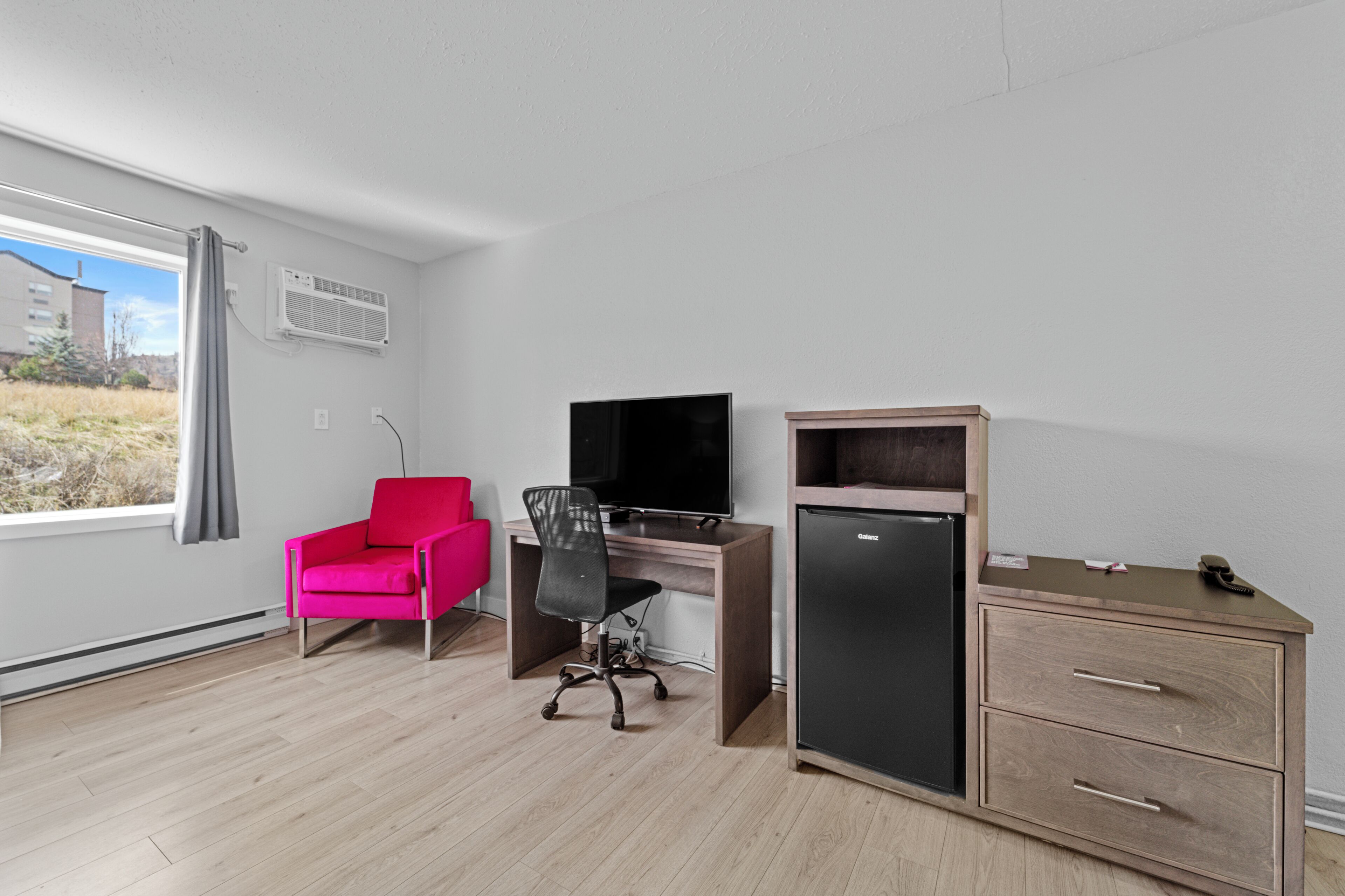 Quarto moderno com escrivaninha, cadeira, televisão e frigorífico.