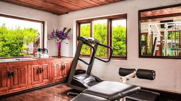 Uma academia com equipamentos de exercícios, armários de madeira e grandes janelas com vista para o verde.