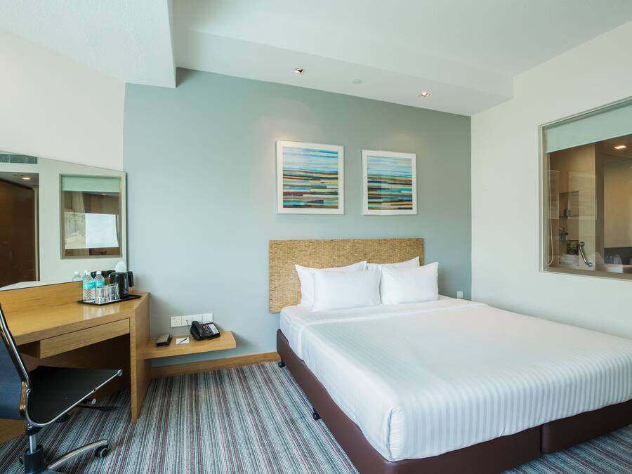 Quarto de hotel com cama, escrivaninha, cadeira e duas obras de arte emolduradas na parede.