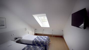 Quarto com duas camas, um claraboia, TV fixada na parede e mesa de cabeceira com abajur.