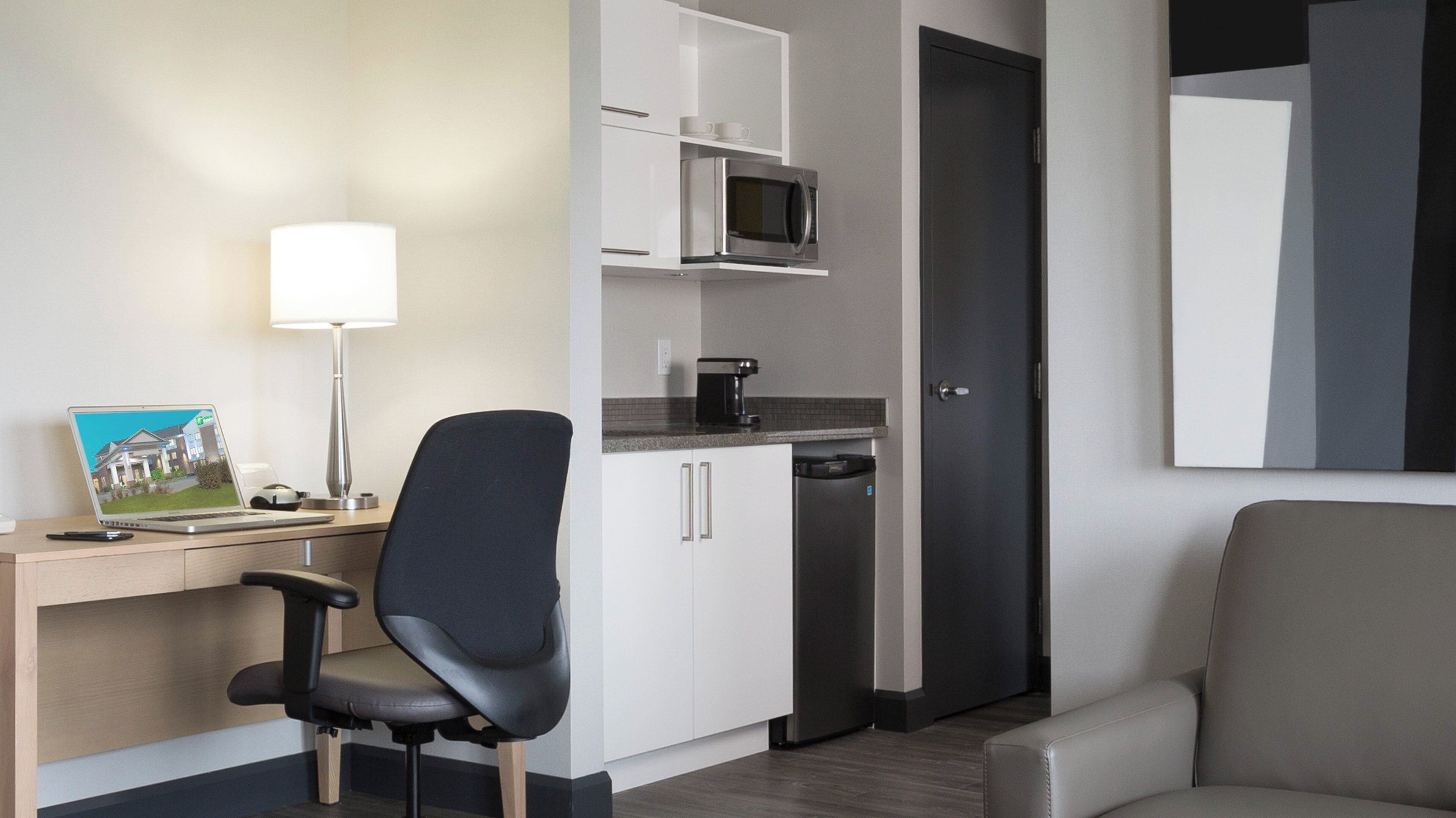 Quarto de hotel com escrivaninha, cadeira, micro-ondas, cafeteira e porta.