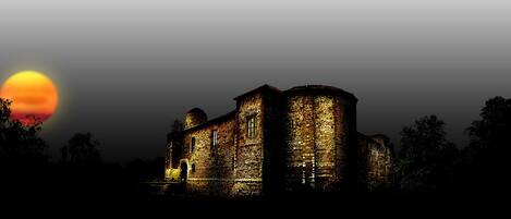 Um edifício histórico com janelas iluminadas e uma torre imponente, sob um céu ao pôr do sol.