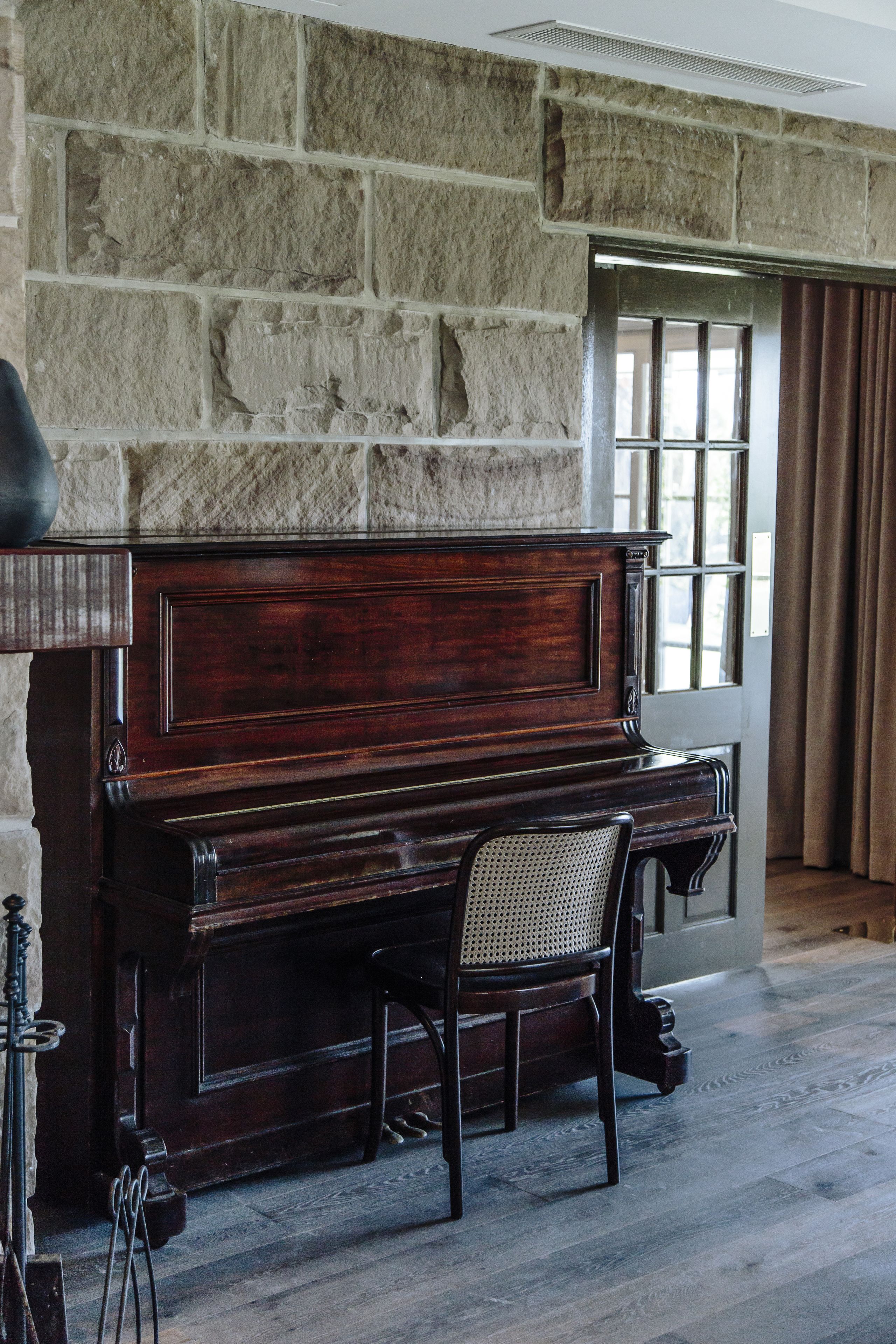Um piano de cauda em um quarto com paredes de pedra e uma janela grande.