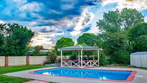 Um quintal com piscina, um gazebo e área cercada.
