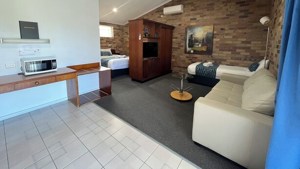 Quarto de hotel moderno com cozinha compacta, sofá, cama e parede de tijolos.