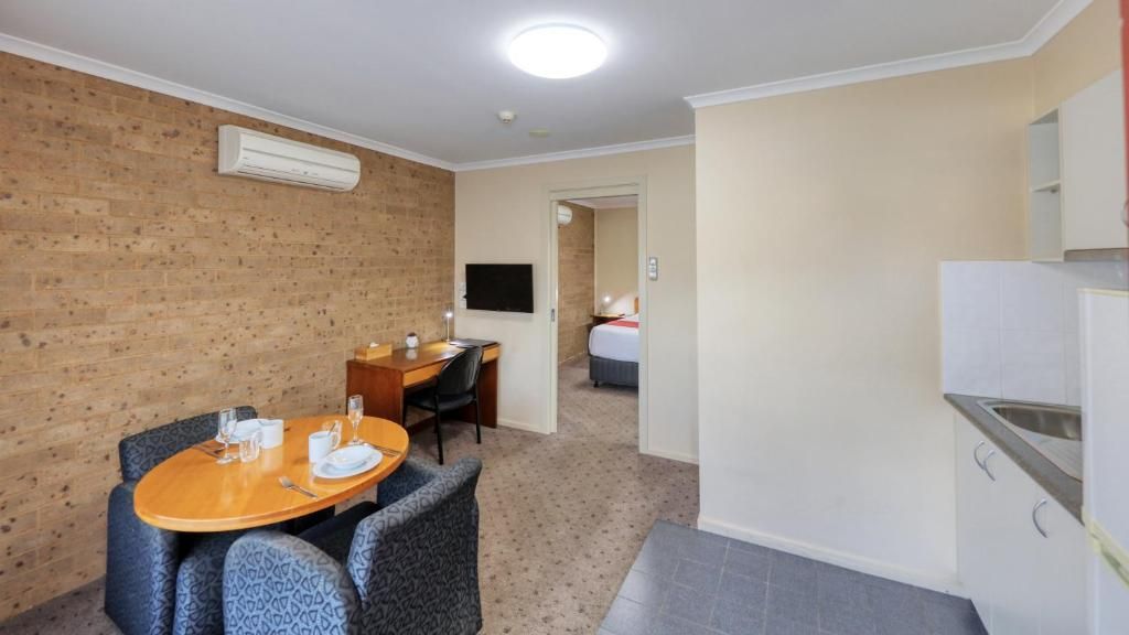 Quarto de hotel compacto com área de jantar, cozinha compacta e uma cama ao fundo.
