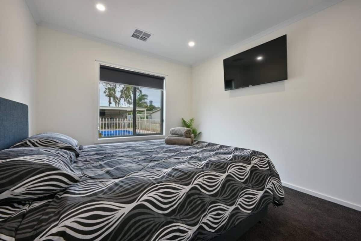 Quarto com uma cama grande, TV fixada na parede e janela com vista para uma piscina e palmeiras.