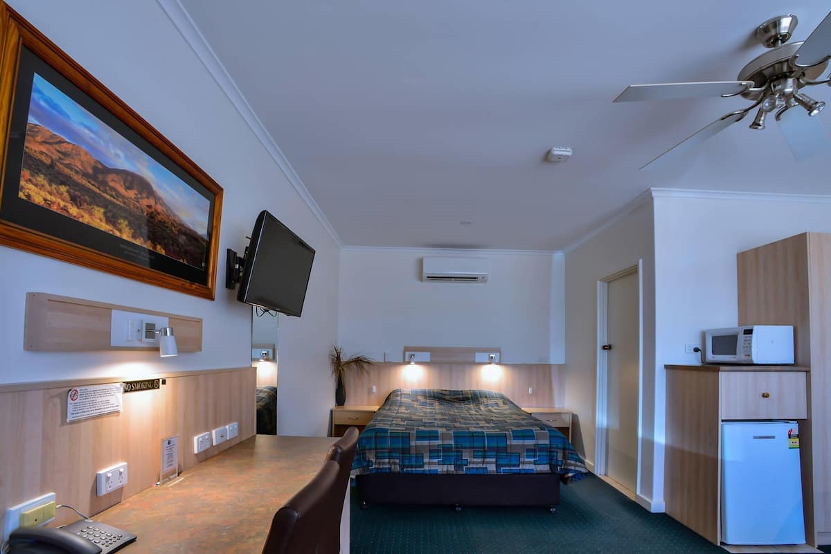 Quarto de hotel com cama, escrivaninha, cadeira, televisão e micro-ondas.