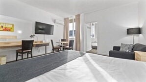 Quarto de hotel com cama, escrivaninha, cadeiras, televisão e sofá.