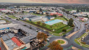 Vista aérea de área comercial com piscina, estacionamentos e um cruzamento rotatório.