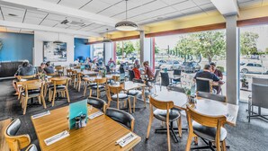 Um restaurante espaçoso com várias mesas e cadeiras, amplas janelas com vista para a rua e decoração de interiores moderna.