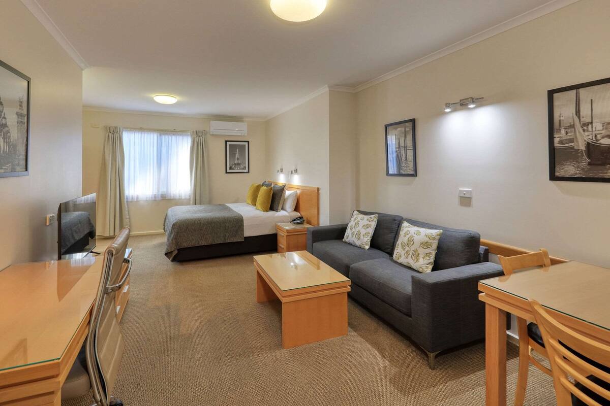 Quarto de hotel com cama, sofá, escrivaninha e televisão.