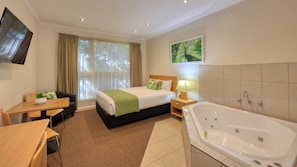 Quarto de hotel com cama, escrivaninha, cadeira, banheiro com banheira e uma grande janela com cortinas.