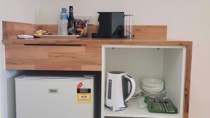 Uma cozinha compacta equipada com micro-ondas, geladeira, chaleira e uma pequena lixeira.