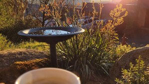 Uma chávena de café numa mesa com vista para um pôr do sol e vegetação circundante.