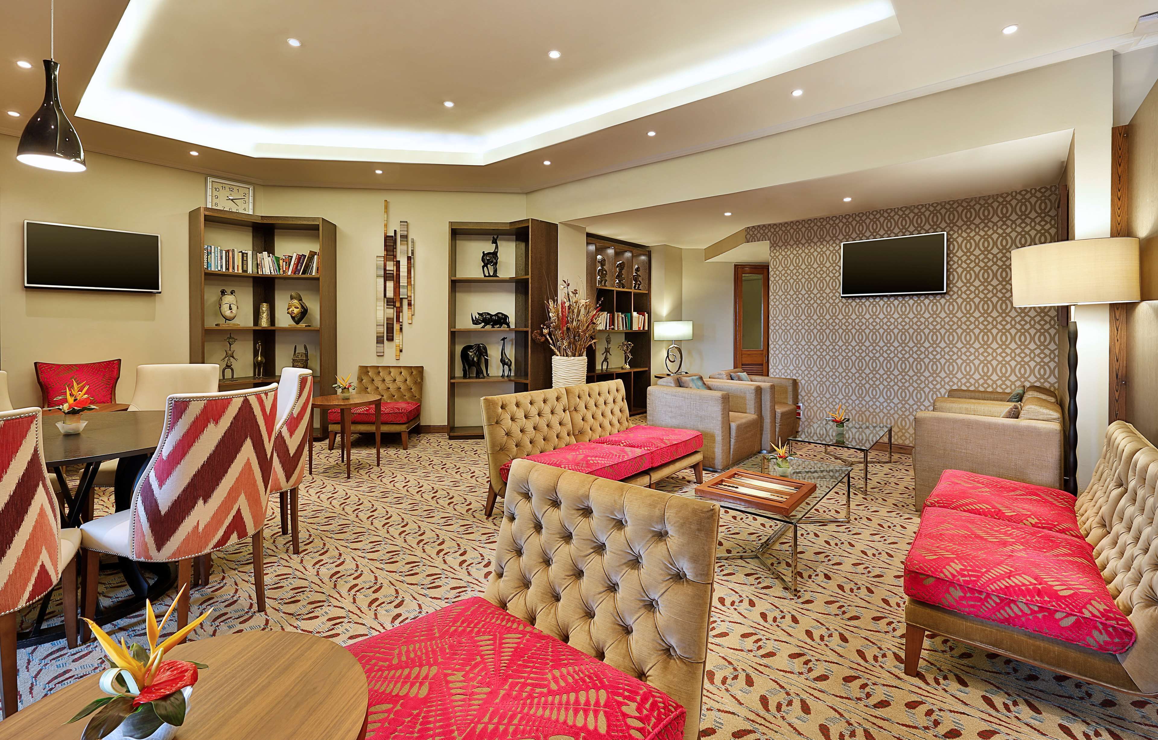 Uma sala de estar ampla, com um sofá grande, um espaço de refeições com mesa e cadeiras, e uma estante cheia de livros e objetos decorativos.