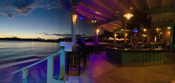 Uma área de bar ao ar livre com vista para a água, mesas, cadeiras e um balcão.