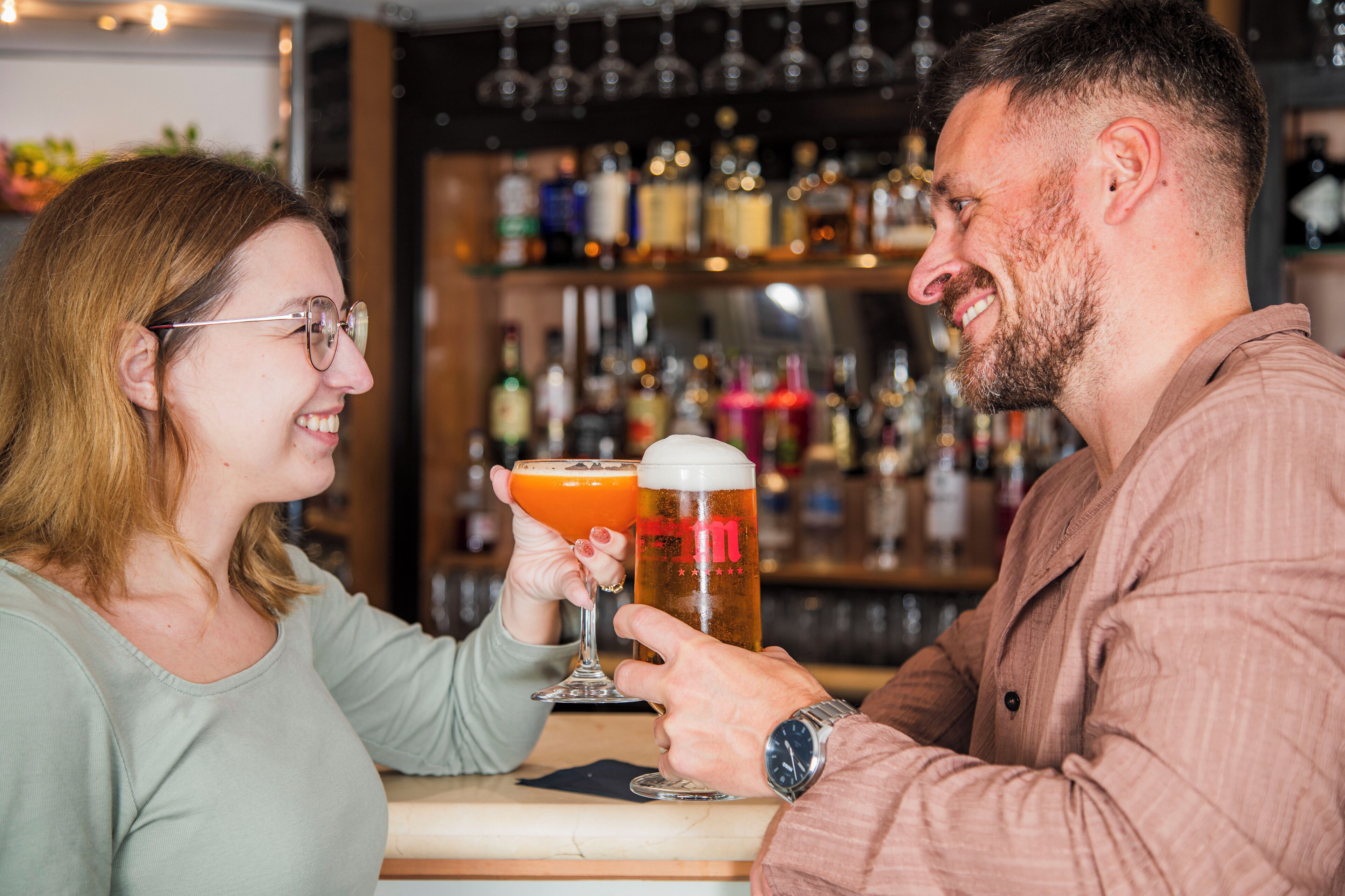 Um bar com uma pessoa segurando um copo de cerveja e outra pessoa com uma bebida.
