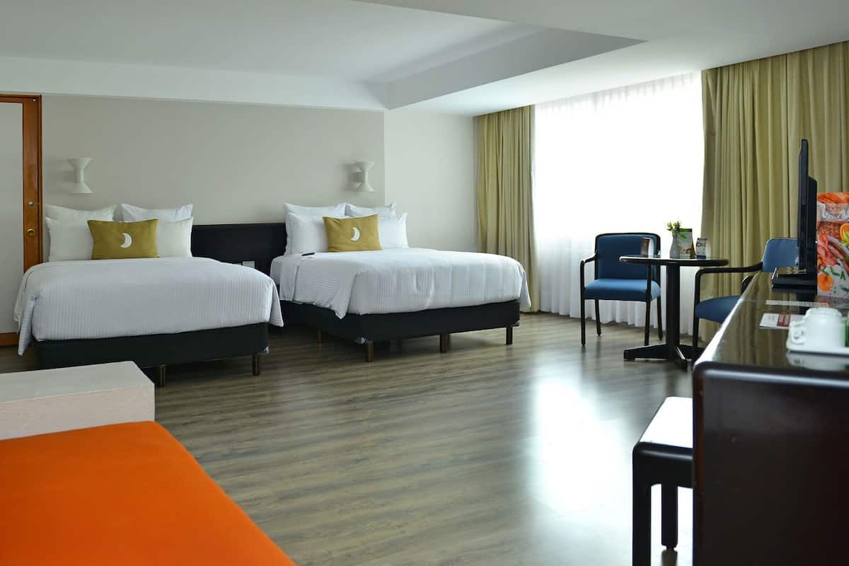 Quarto de hotel com duas camas, uma escrivaninha, uma cadeira e um sofá.