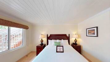 Quarto de hotel com uma cama grande, duas mesas de cabeceira com luminárias, uma janela com vista e um quadro na parede.