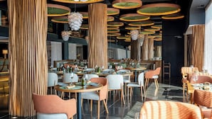 Interior moderno de restaurante com mesas redondas, cadeiras estofadas e design de teto original.