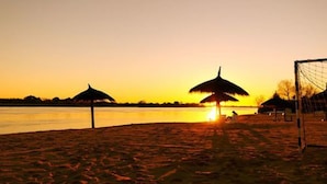 Uma praia com dois guarda-sóis de palha e um gol, remetendo a um campo esportivo.