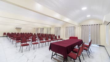 Uma sala de conferências com fileiras de cadeiras vermelhas, uma mesa comprida e teto alto.