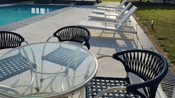 Área da piscina com espreguiçadeiras e mesa sob um toldo.