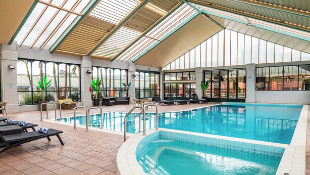 Piscina interior com piso revestido, áreas iluminadas pelo sol e espreguiçadeiras.