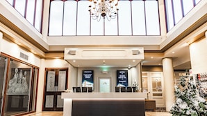 Um saguão de hotel com uma recepção, um candelabro, uma grande janela e um pinheiro de Natal.