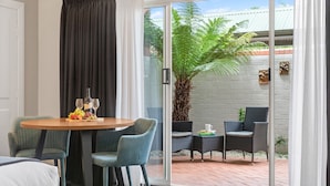 Quarto com mesa de jantar posta para dois, sofá e pequena varanda com mobiliário de exterior.
