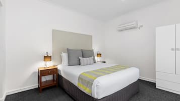 Quarto de hotel com cama, mesas de cabeceira, luminária, ar condicionado e guarda-roupa.