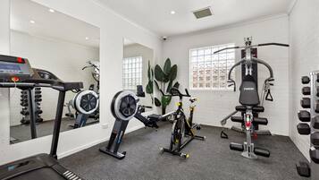 Uma academia com equipamentos de exercício, esteira, bicicleta ergométrica e suporte para pesos.