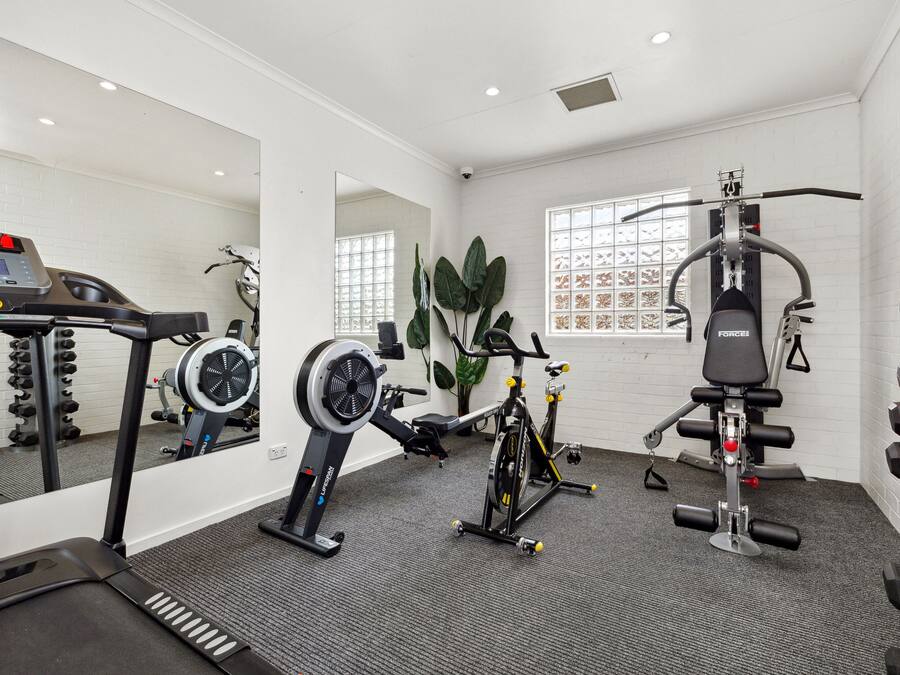 Uma academia com equipamentos de exercício, esteira, bicicleta ergométrica e suporte para pesos.