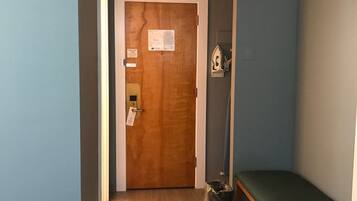 Um quarto com porta de madeira, um banco, uma lixeira e uma pequena mesa.