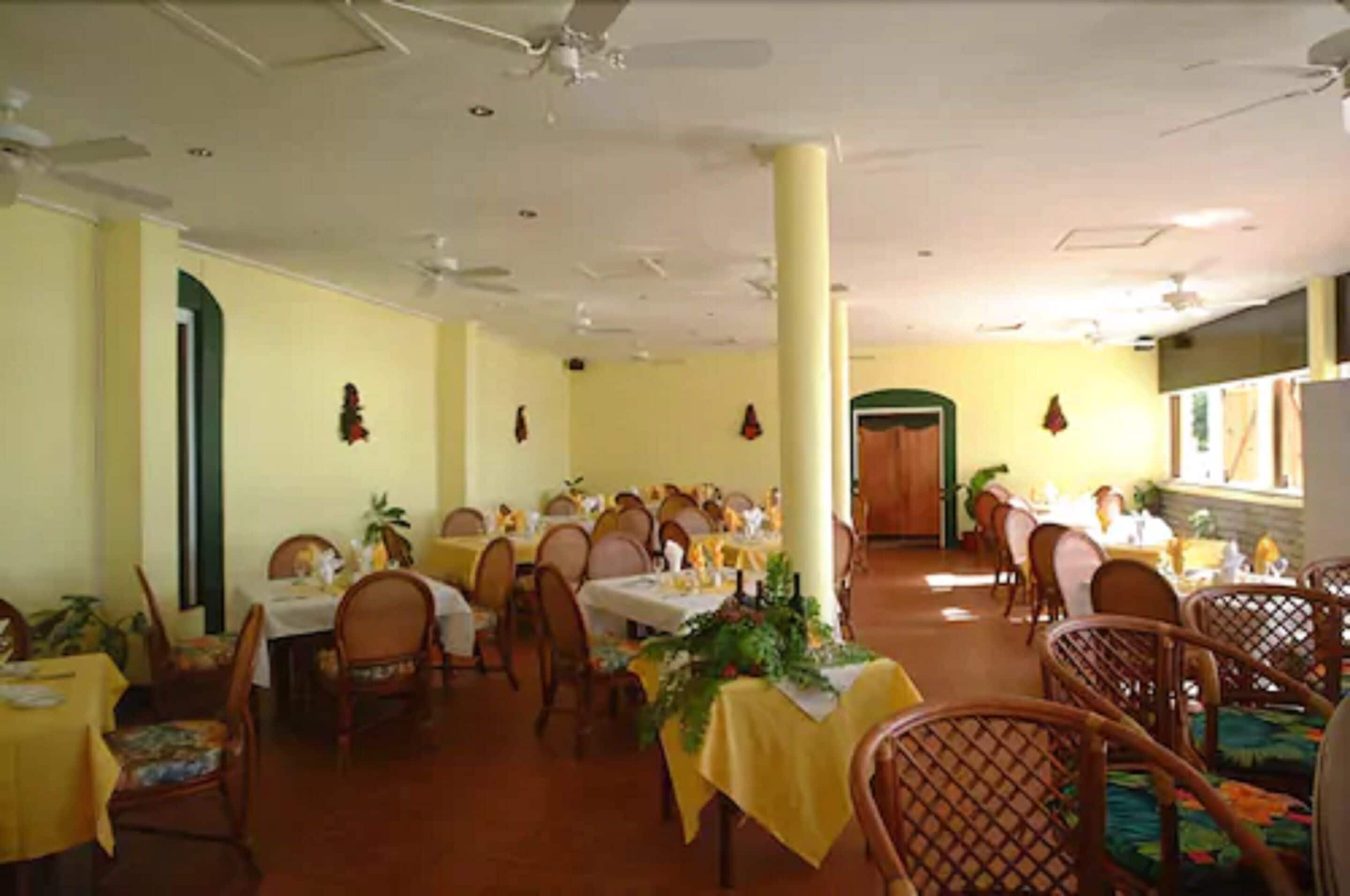 Uma sala de jantar com mesas montadas para vários convidados, cadeiras e ventiladores de teto.