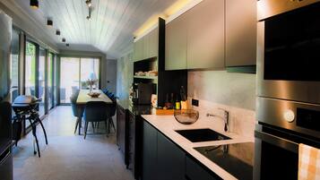 Uma cozinha moderna com uma ilha grande, eletrodomésticos de aço inoxidável e vista para a área de refeições ao ar livre.